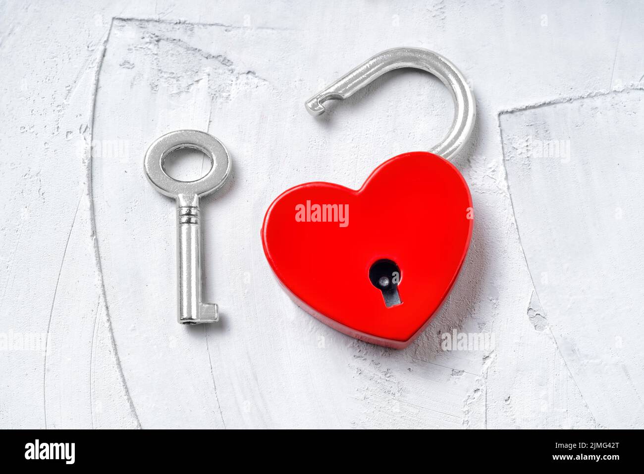 Open red heart-shaped padlock with a silver-toned key on a concrete ...