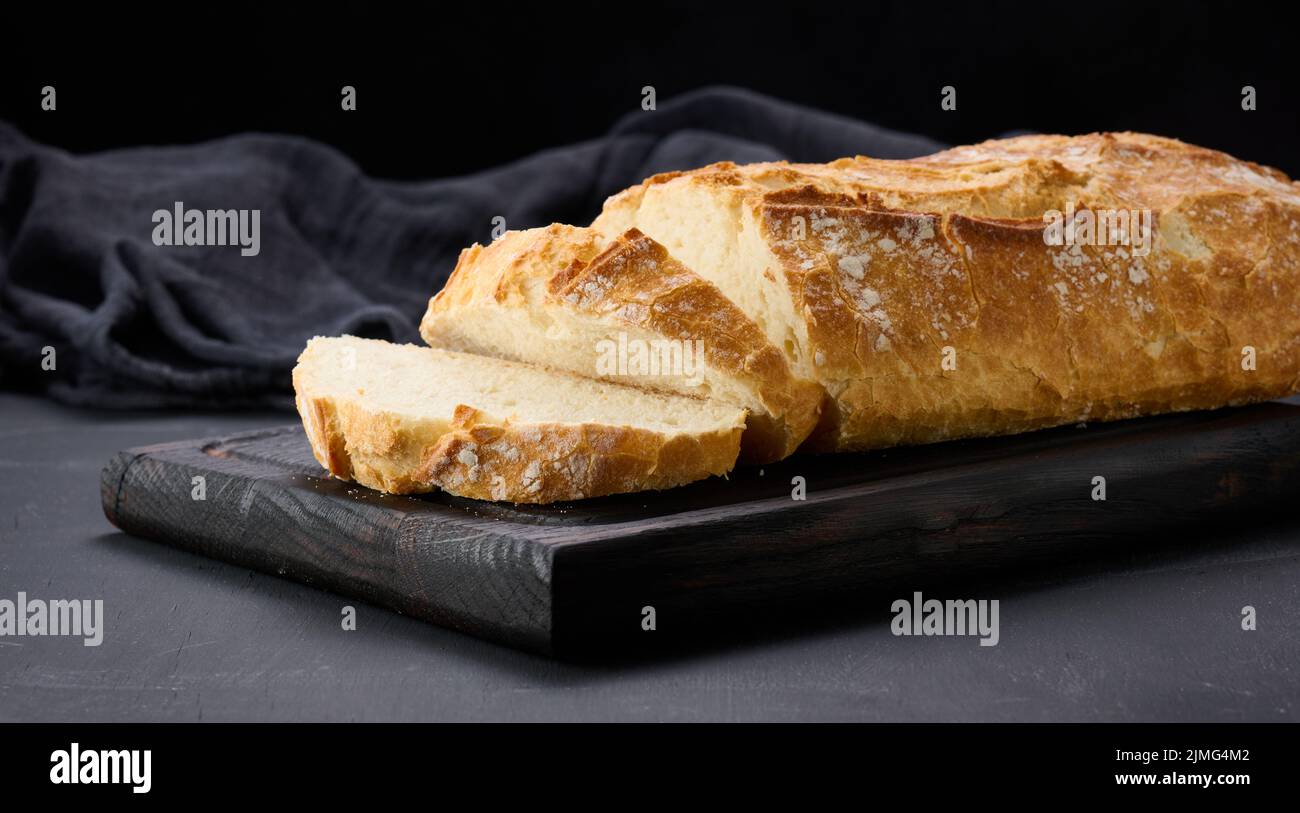 Baked whole oval bread made from white wheat flour on a black table ...