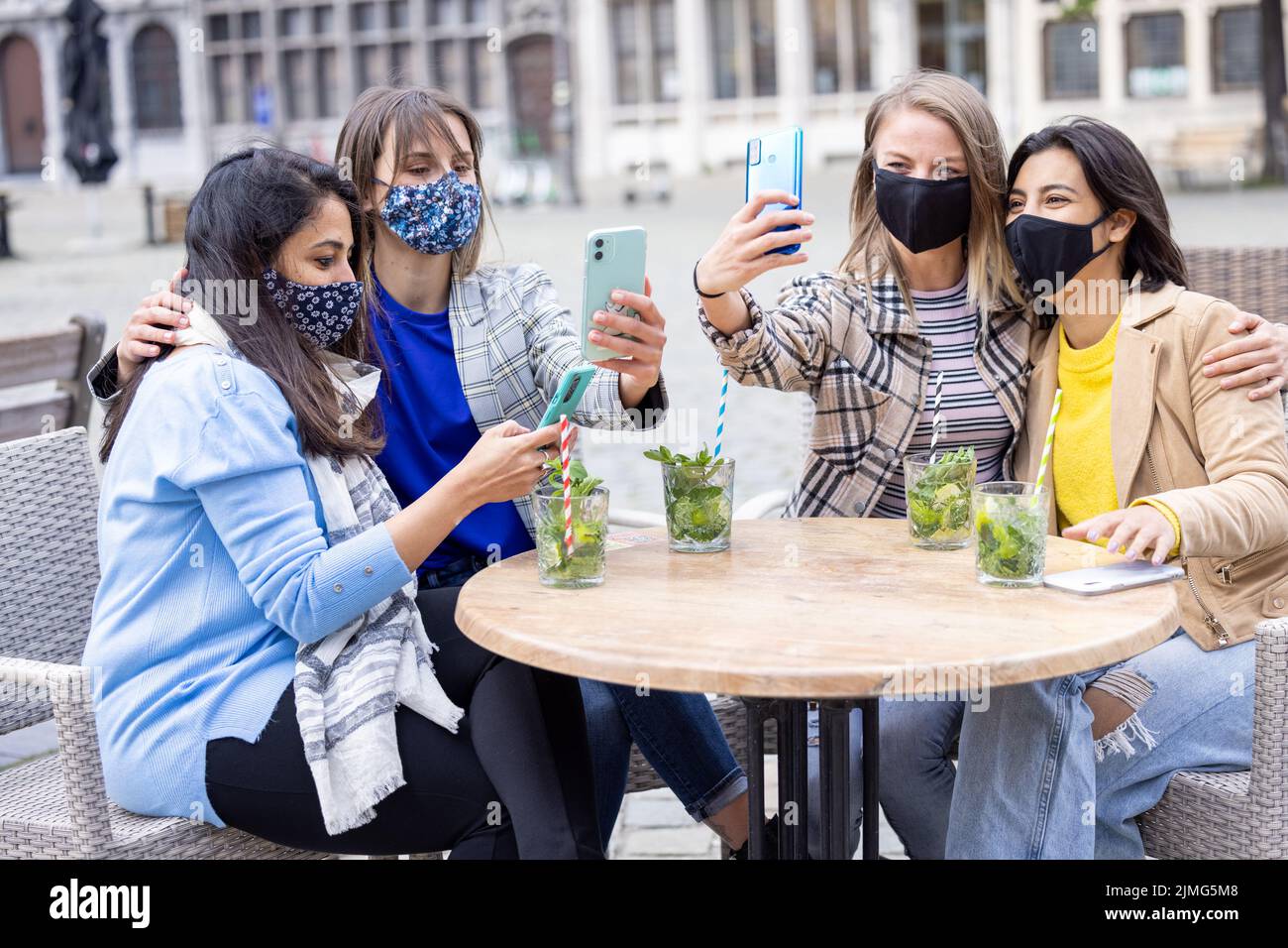 Multiracial Young Female Friends Wearing Facemasks Using Mobile