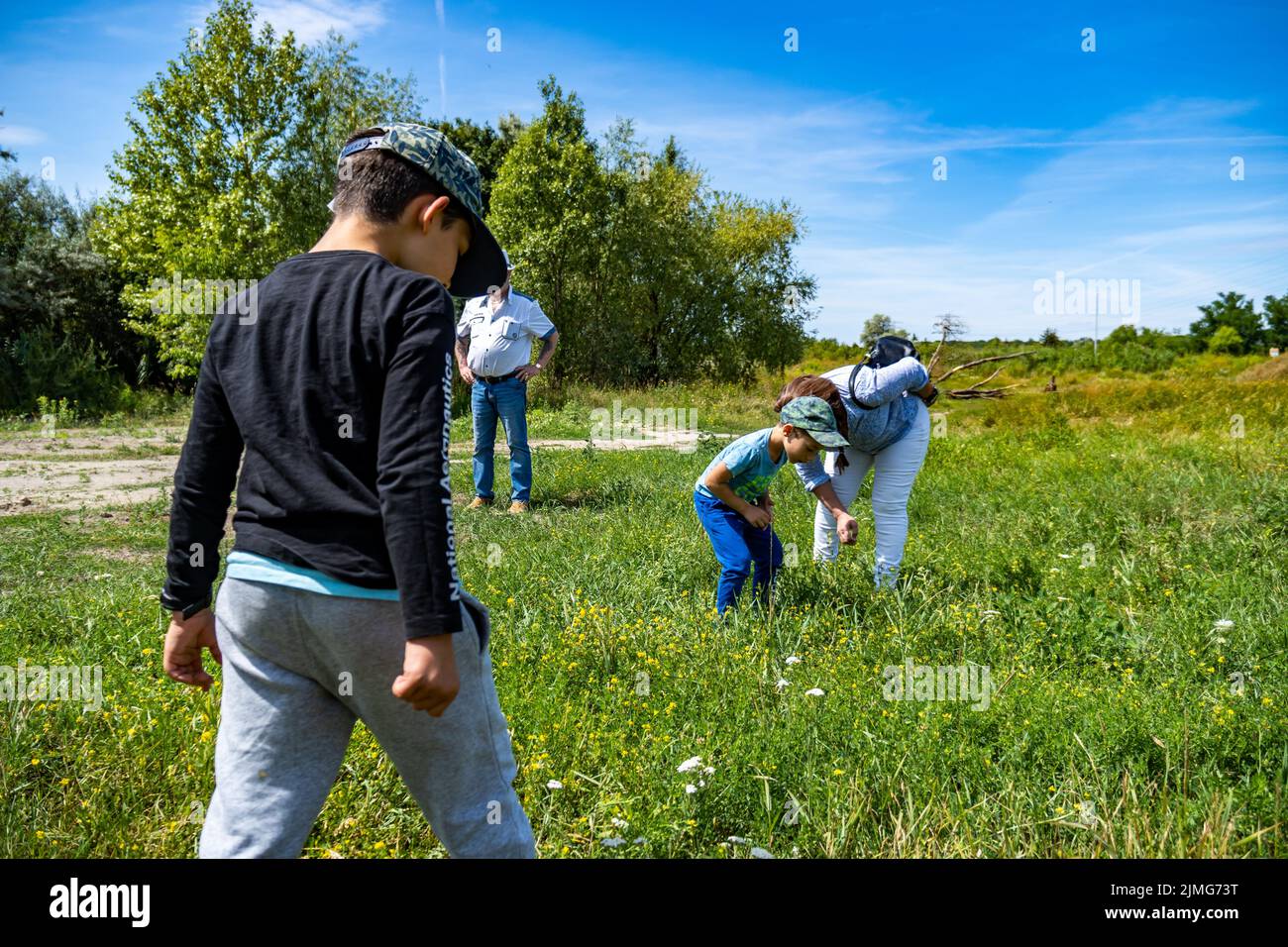 Adults and two children looking for something in green grass and weeds ...