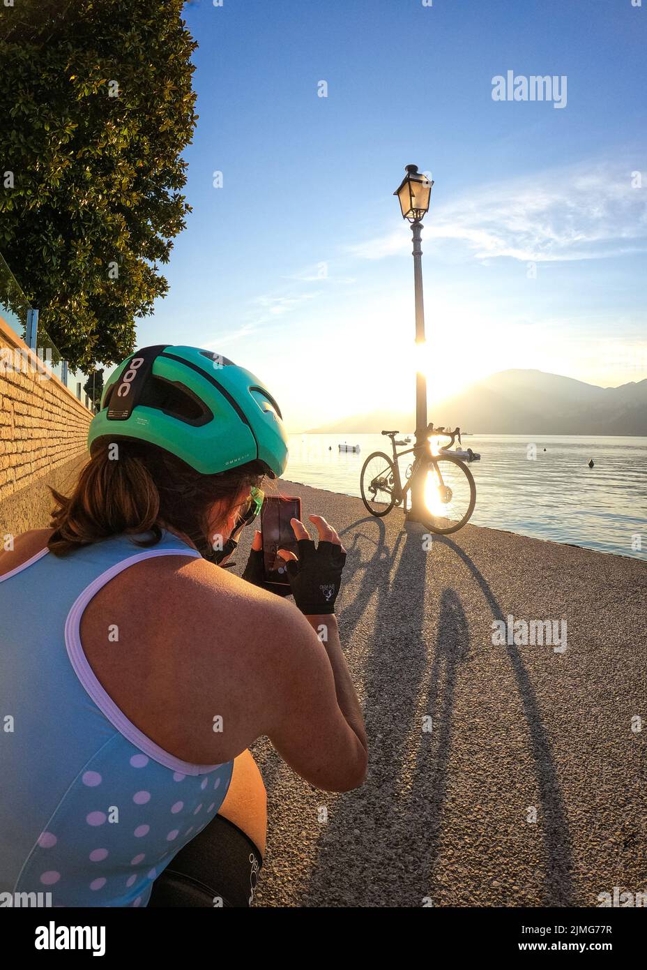 Female cyclist taking picture of her bike. Sunset on lake Garda. Road ...
