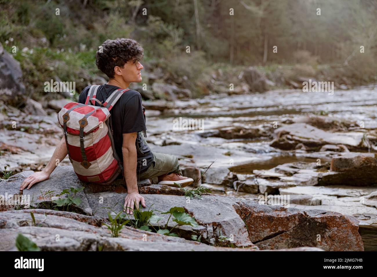 Back view on Caucasian young traveler resting by river in mountains and ...