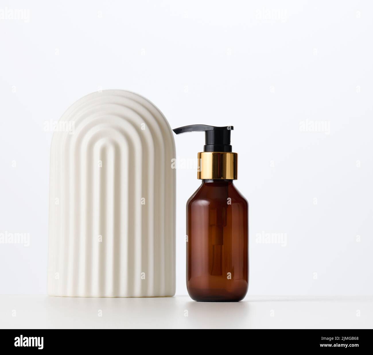 Brown glass bottle with black pump of cosmetic products on white table ...