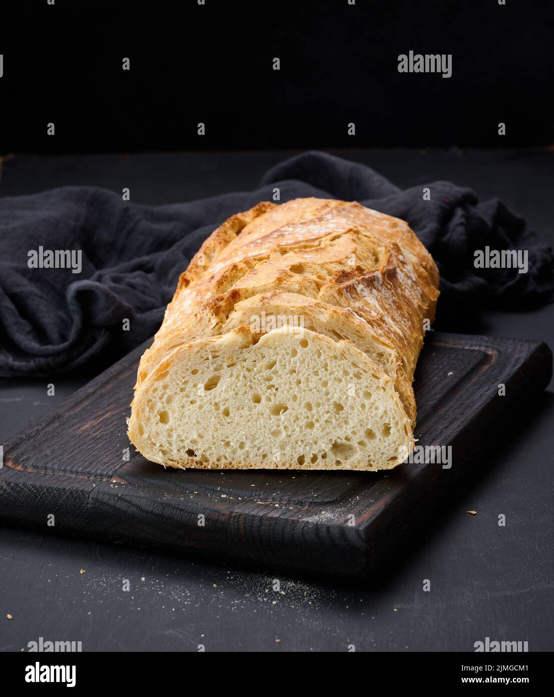 Baked whole oval bread made from white wheat flour on a black table ...