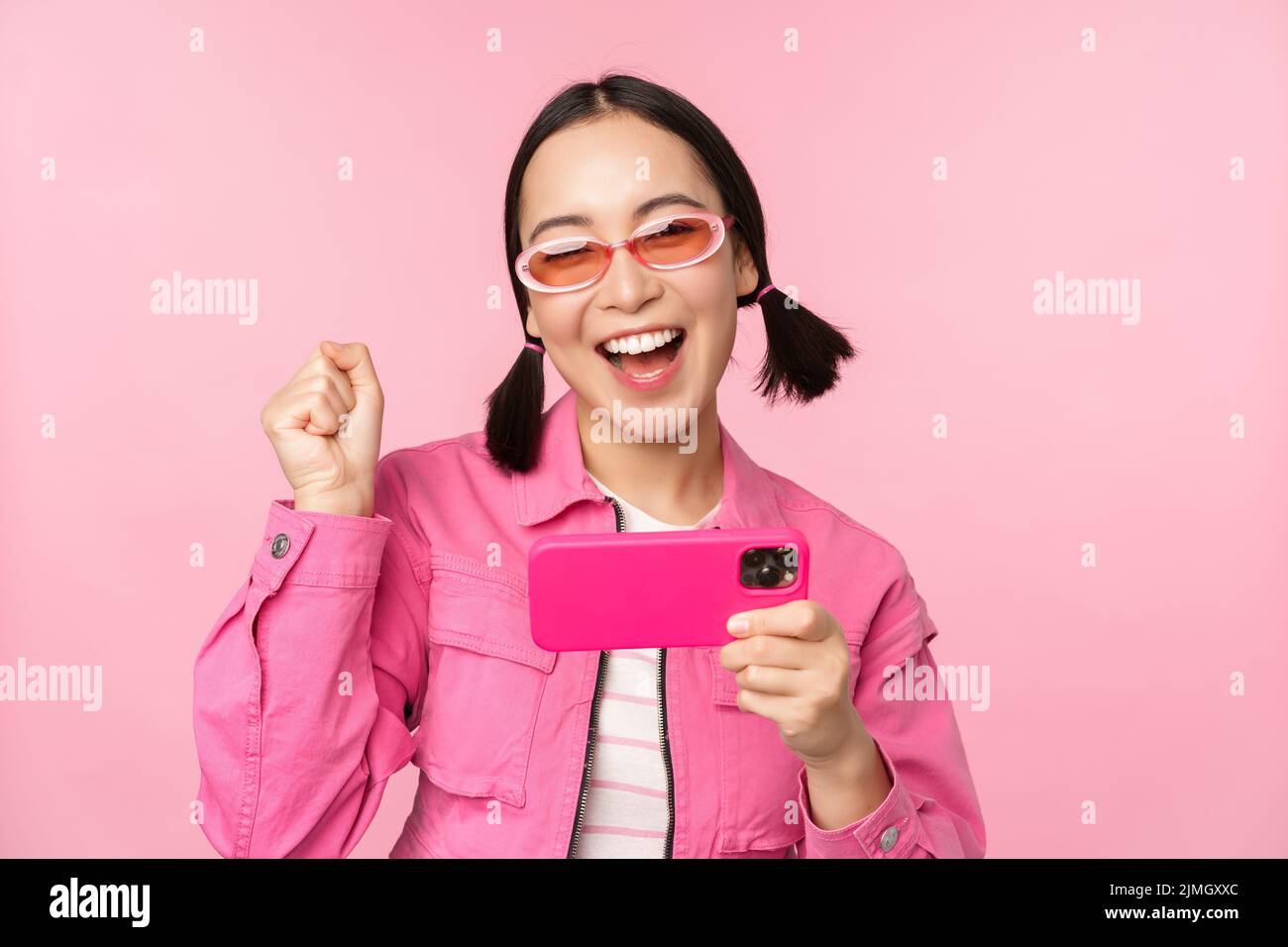Happy smiling korean girl winning on mobile phone, looking at ...
