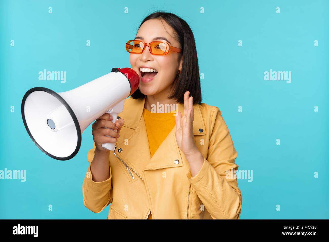 Stylish asian girl making announcement in megaphone, shouting with ...