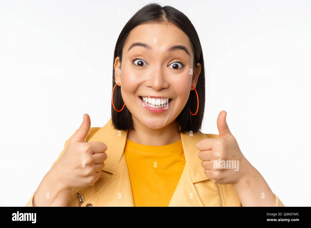 Smiling asian girl showing thumbs up, looking pleased, approve smth ...