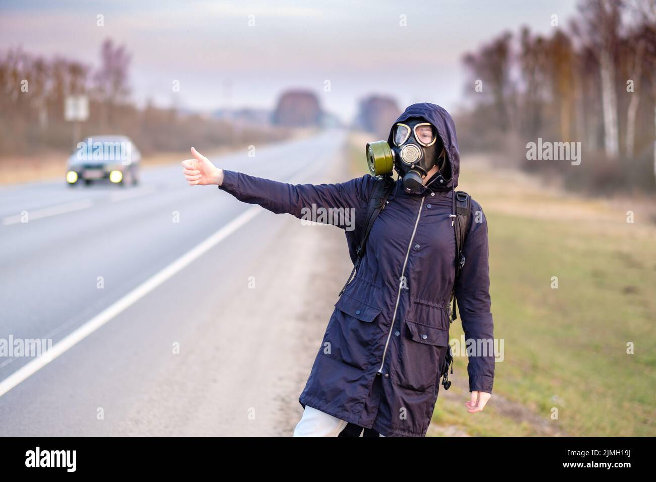 A girl in dark clothes, a gas mask and a hood on her head raises her ...