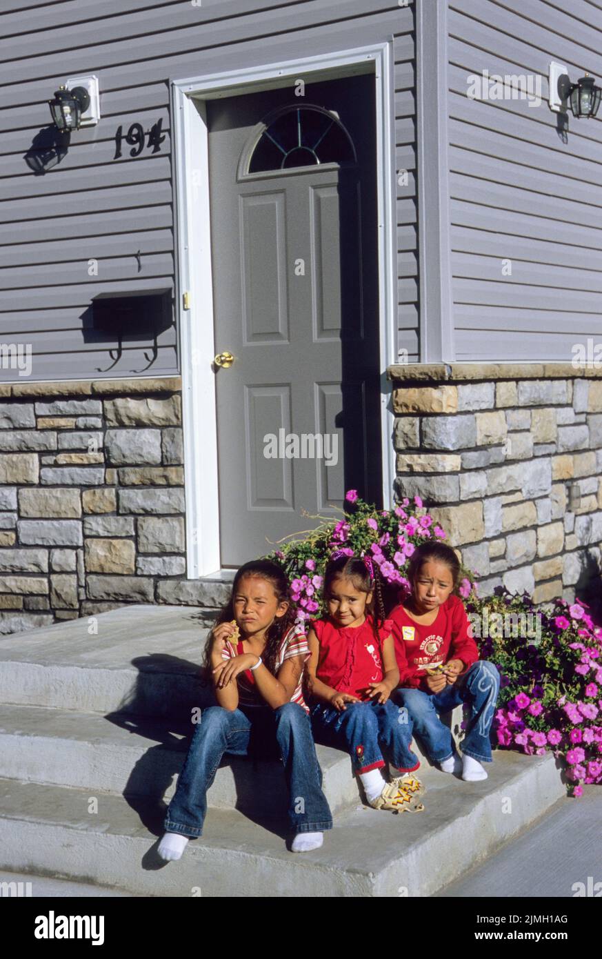 Three Native American children sit on steps next to a doorway in front ...