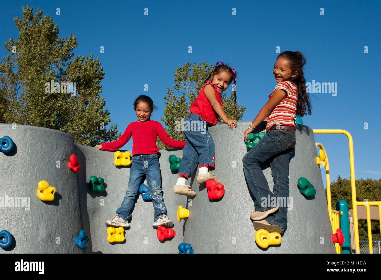 Three Native American elementary age girls climb up on wall outside at ...