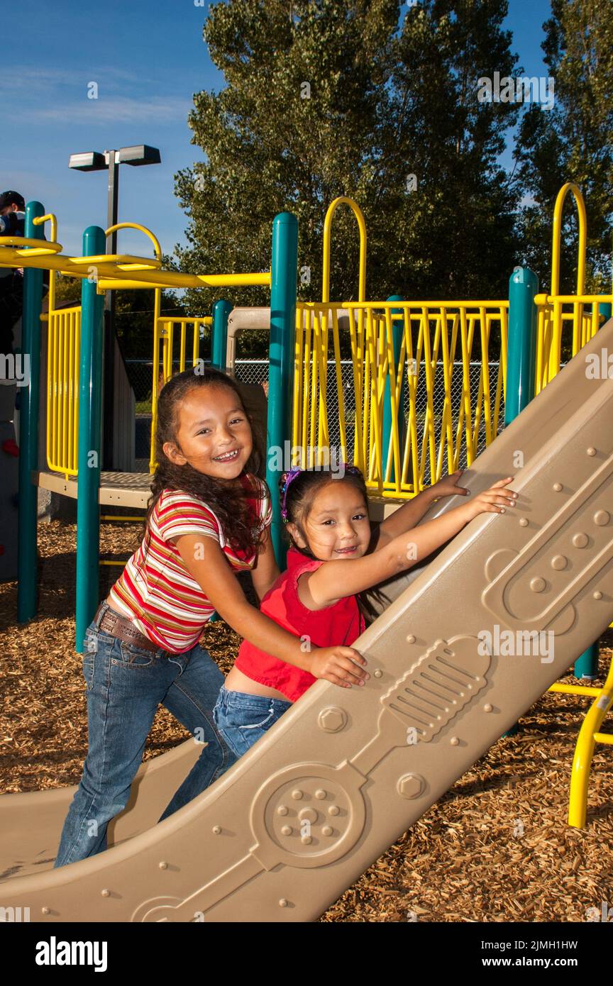 Two Native American elementary age girls climb up a slide playground ...