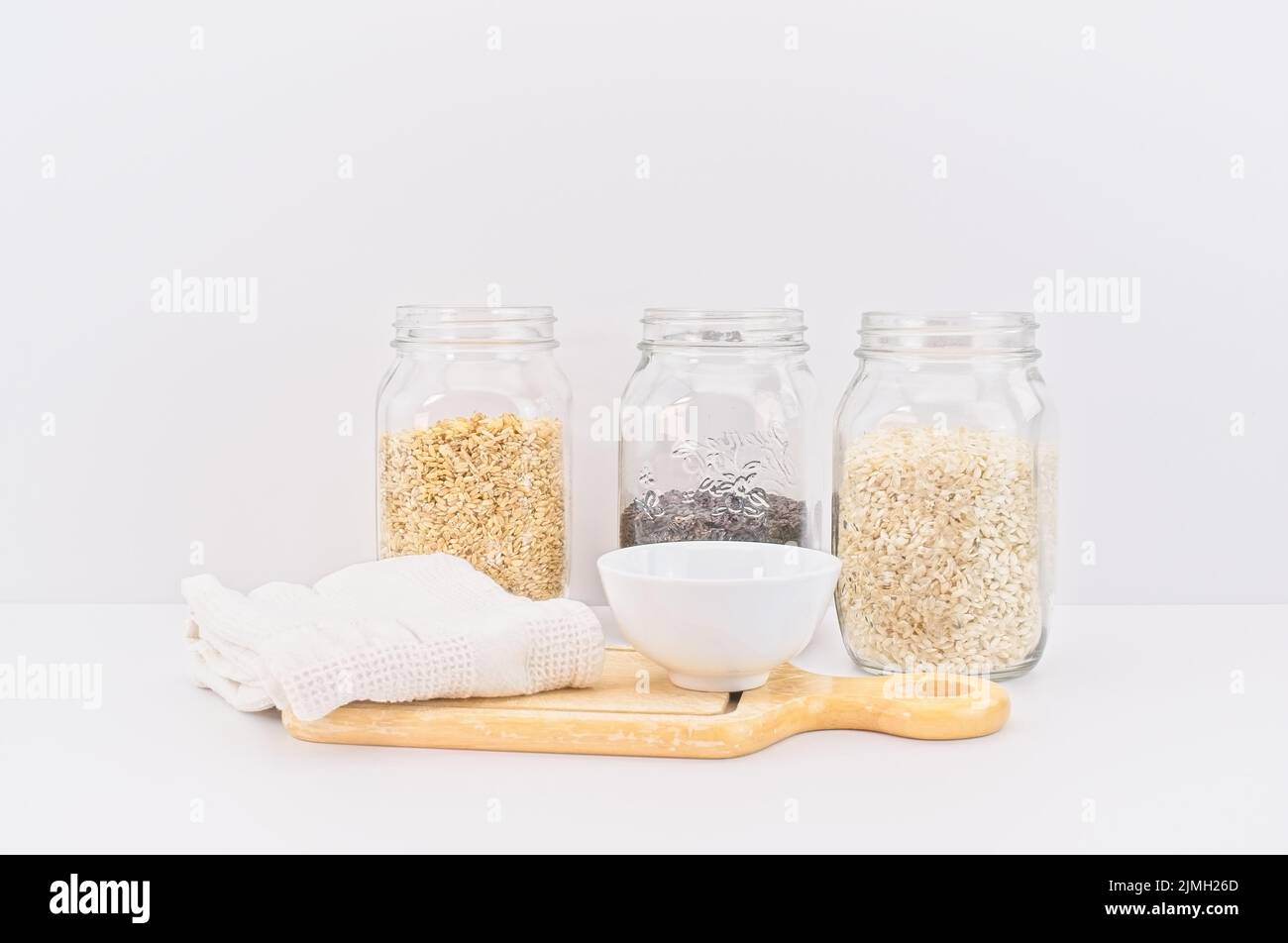 glass jar and containers with organic farming rice on a white table and ...