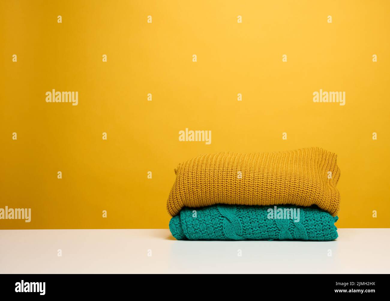 Stack of washed folded clothes on a white table, yellow background ...