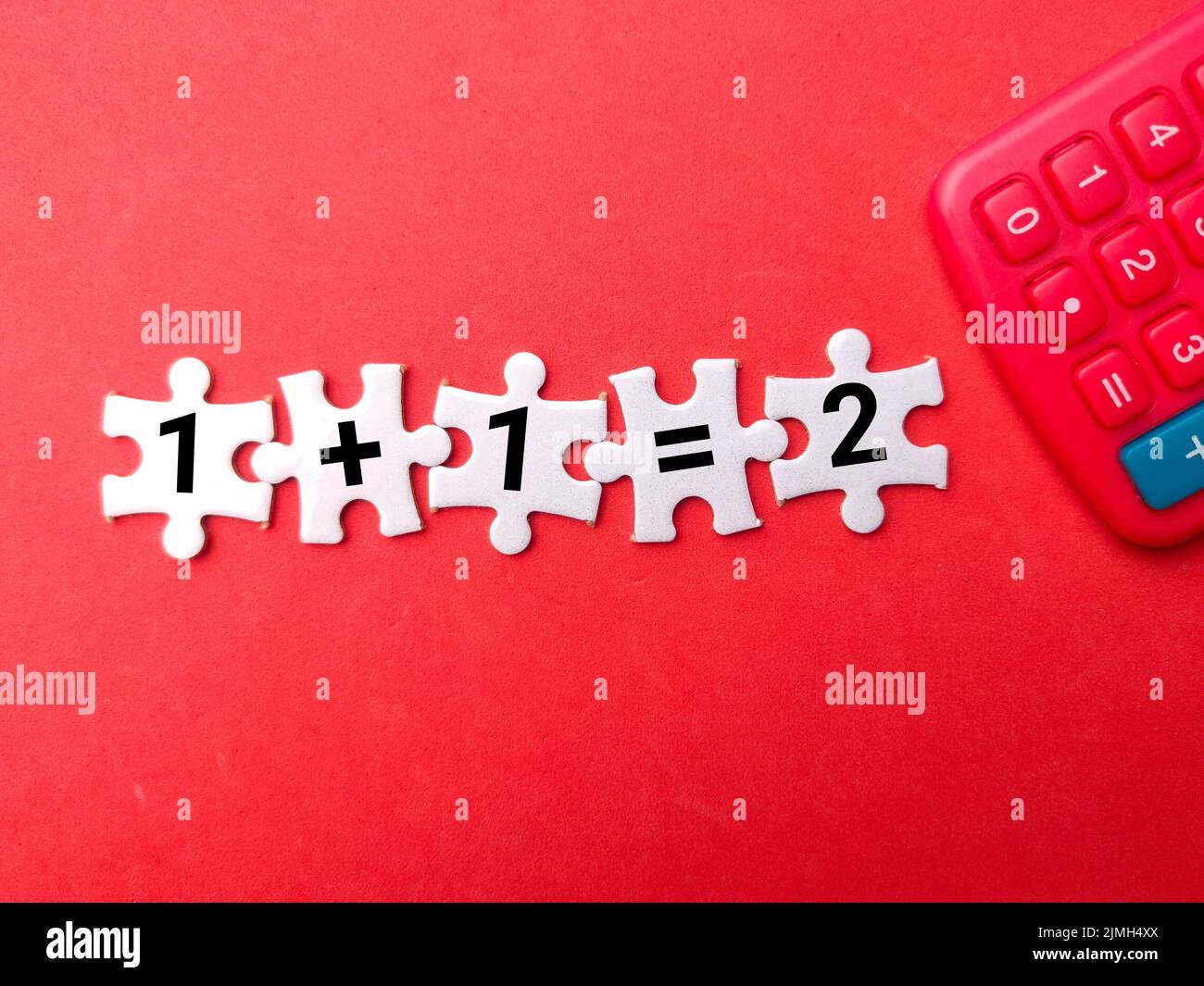White puzzles and calculator with number 1 plus 1 equal to 2 on red ...