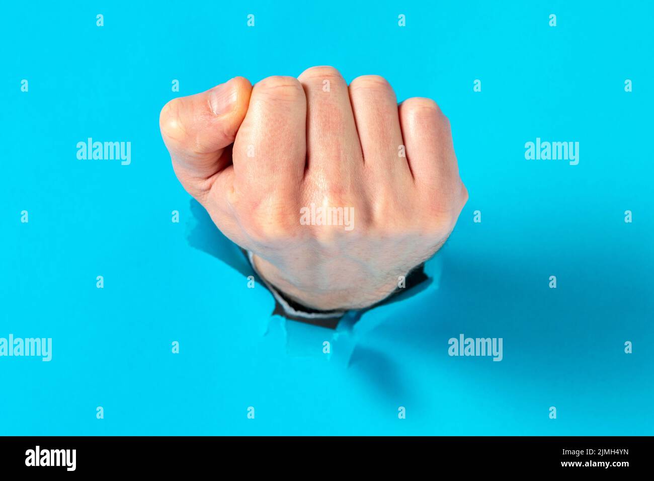 Man breaking through blue paper with fist Stock Photo - Alamy