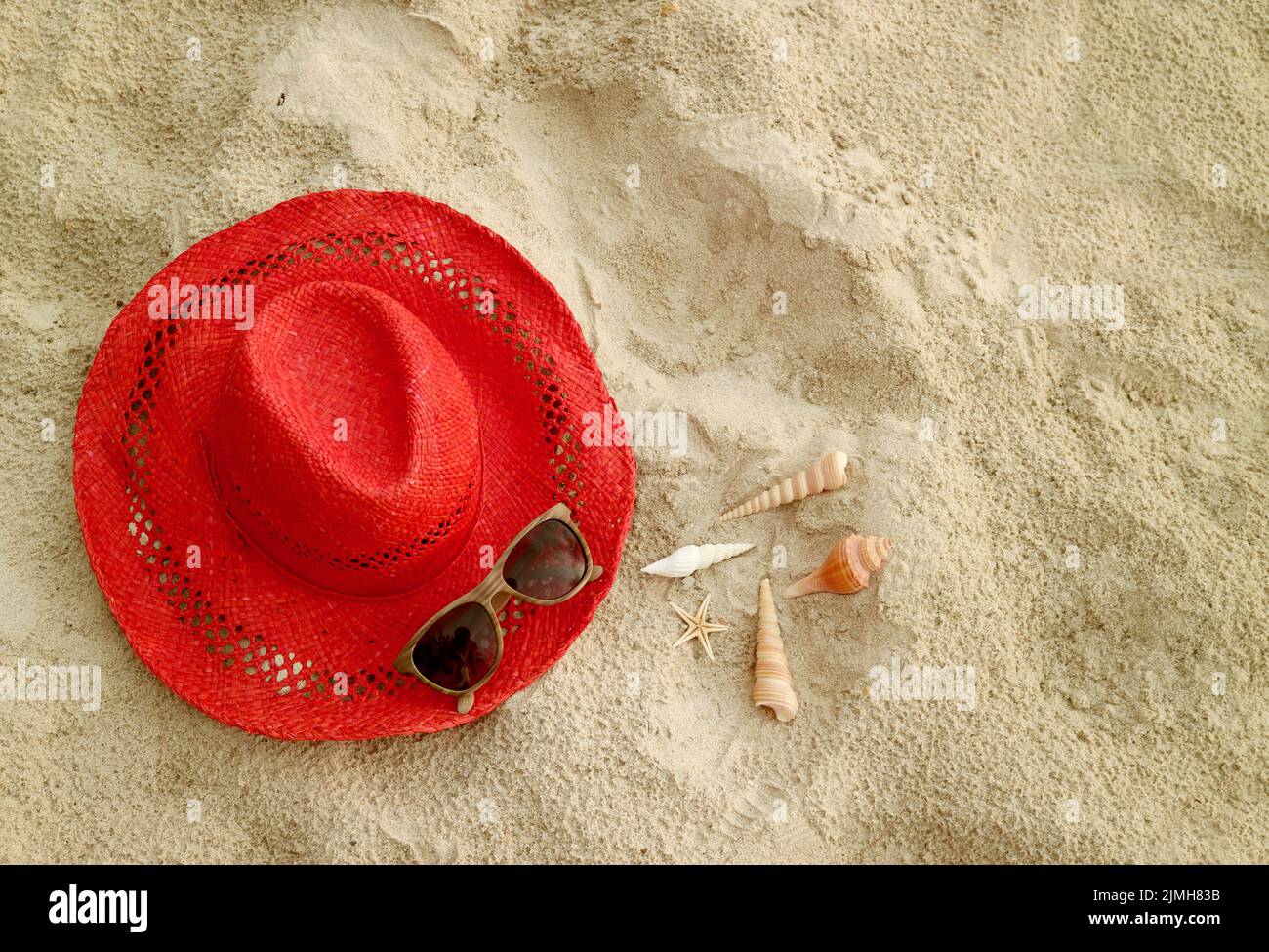 Red straw hat and sunglasses on the sandy beach with tiny seashells ...