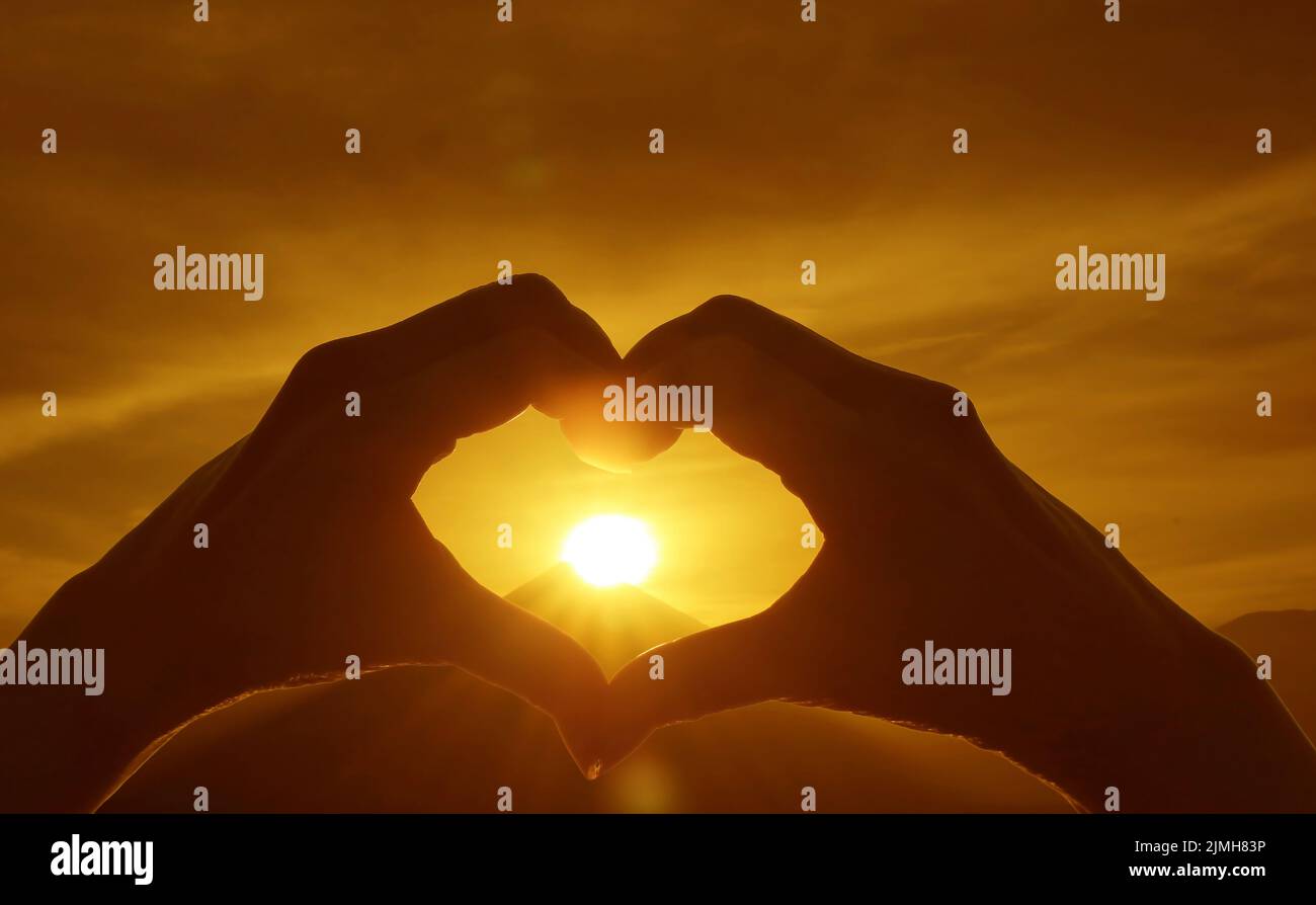 Silhouette of hand making heart sign to the bright sun rising over the ...