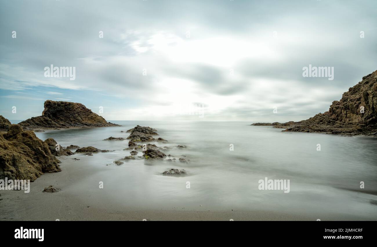 Long exposure of a picturesque small beach in a rocky cove with reef at ...