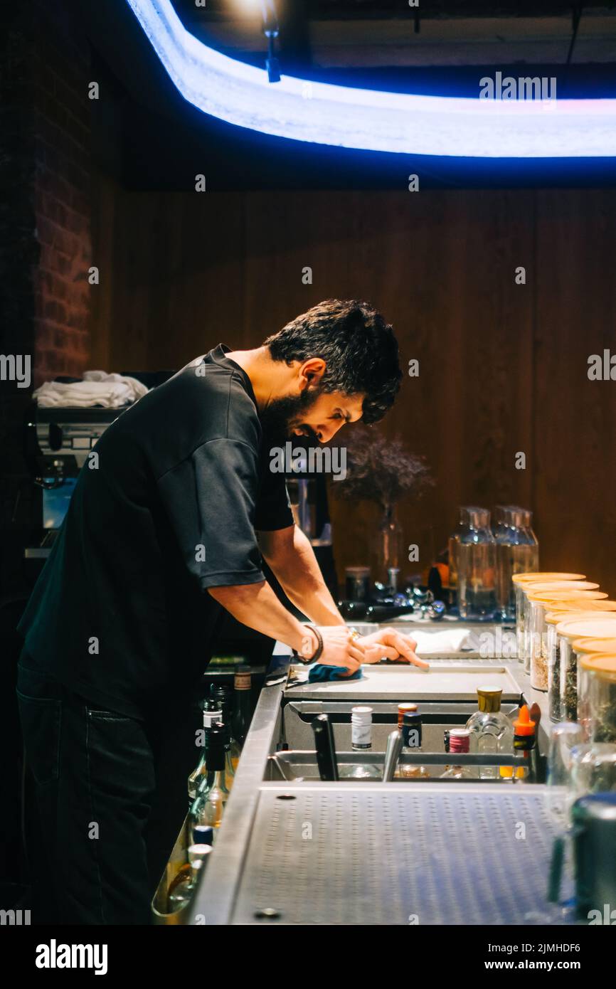Young caucasian man asian bistro worker cleaning table on the bar ...