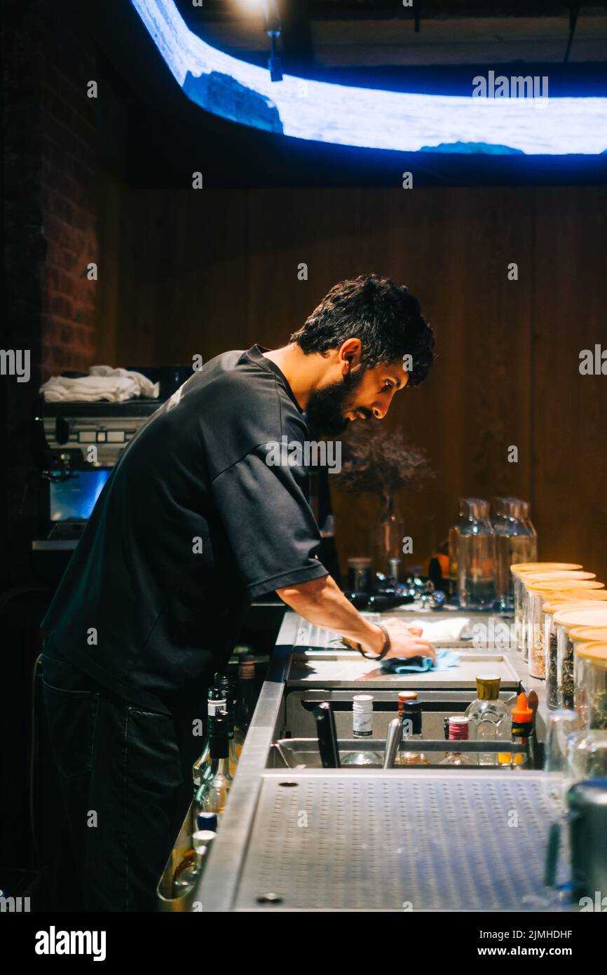 Young caucasian man asian bistro worker cleaning table on the bar ...