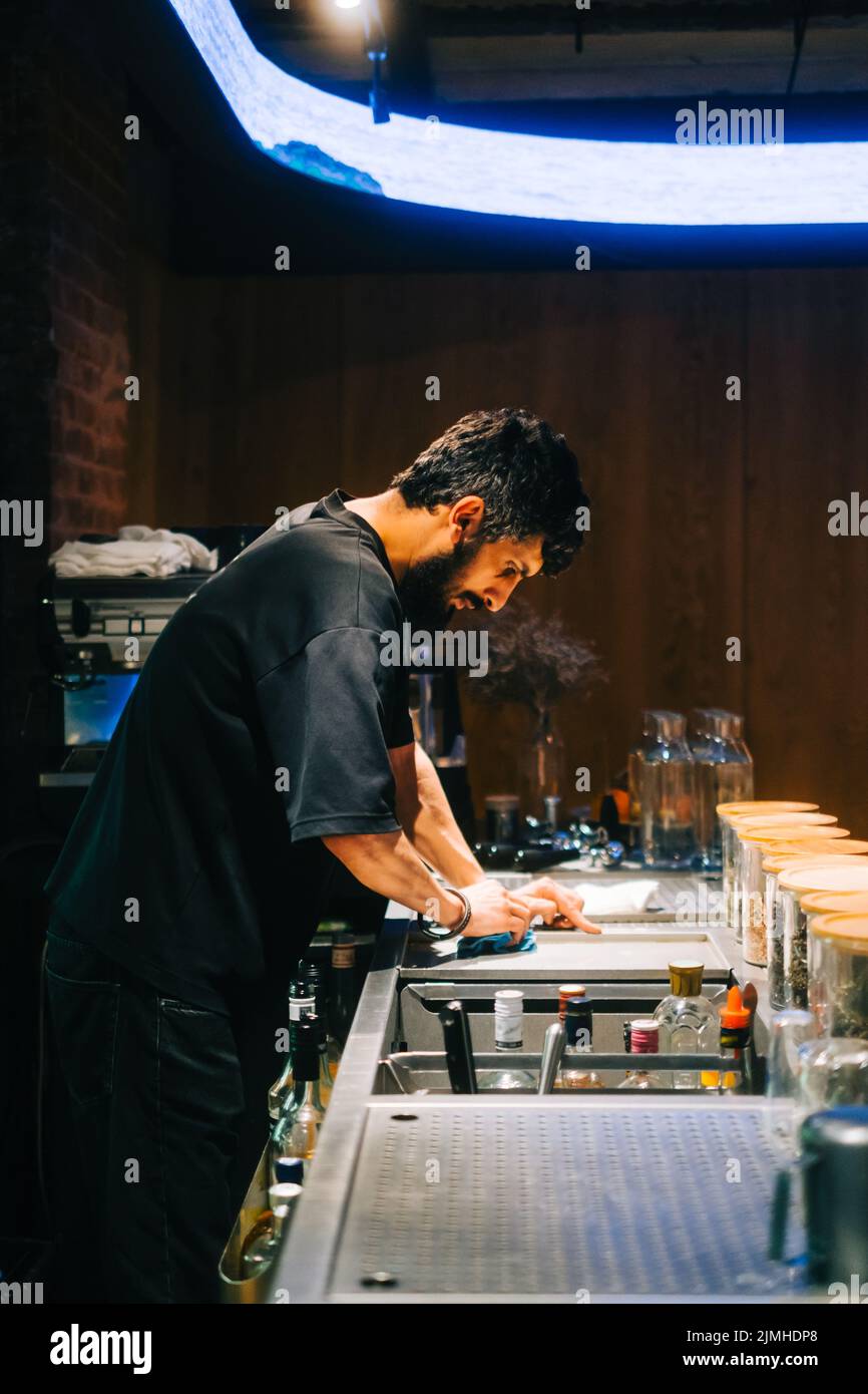 Young caucasian man asian bistro worker cleaning table on the bar ...