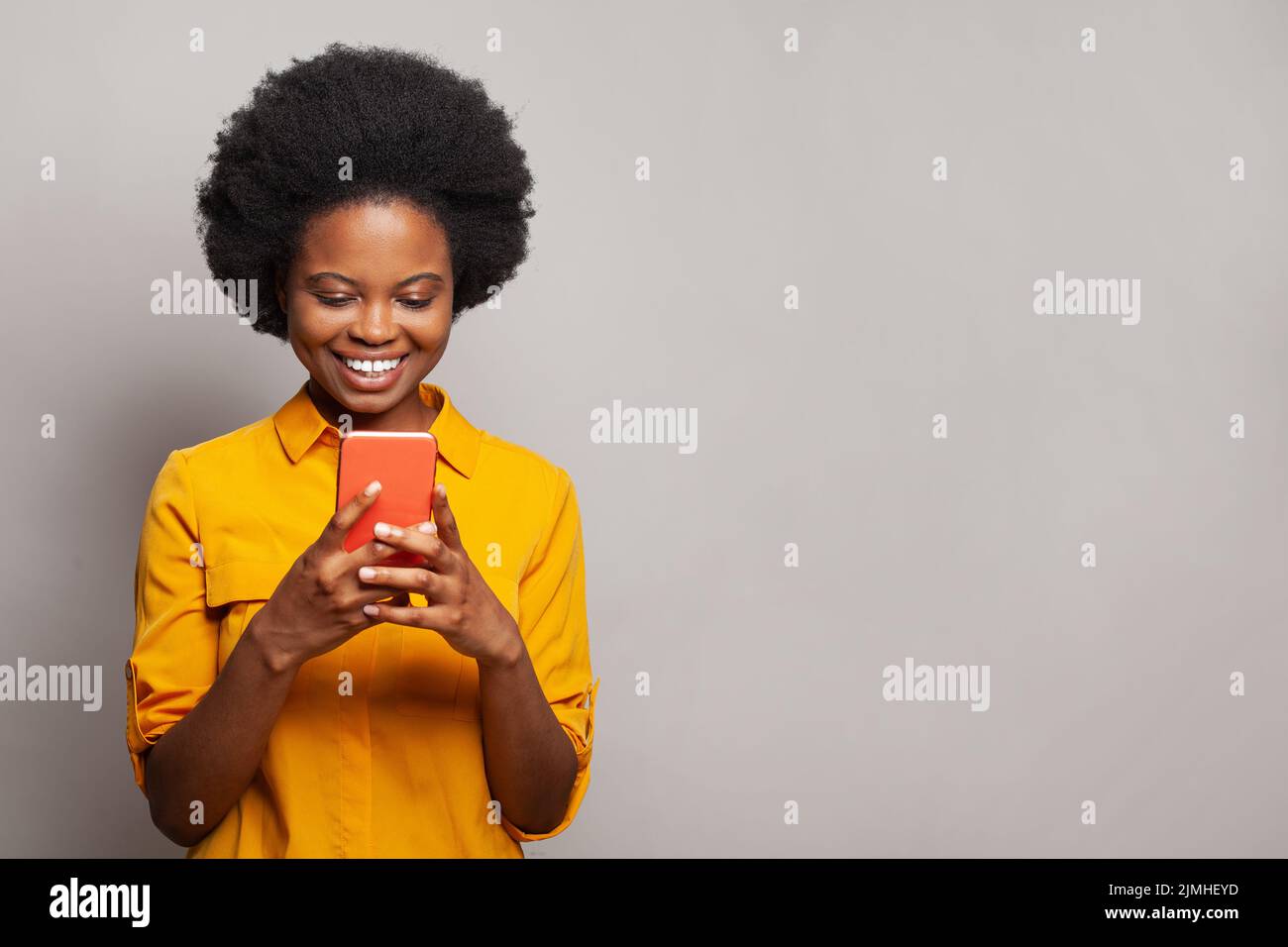 Smiling woman texting on her phone. Happy black model using smartphone, messaging or browsing ...