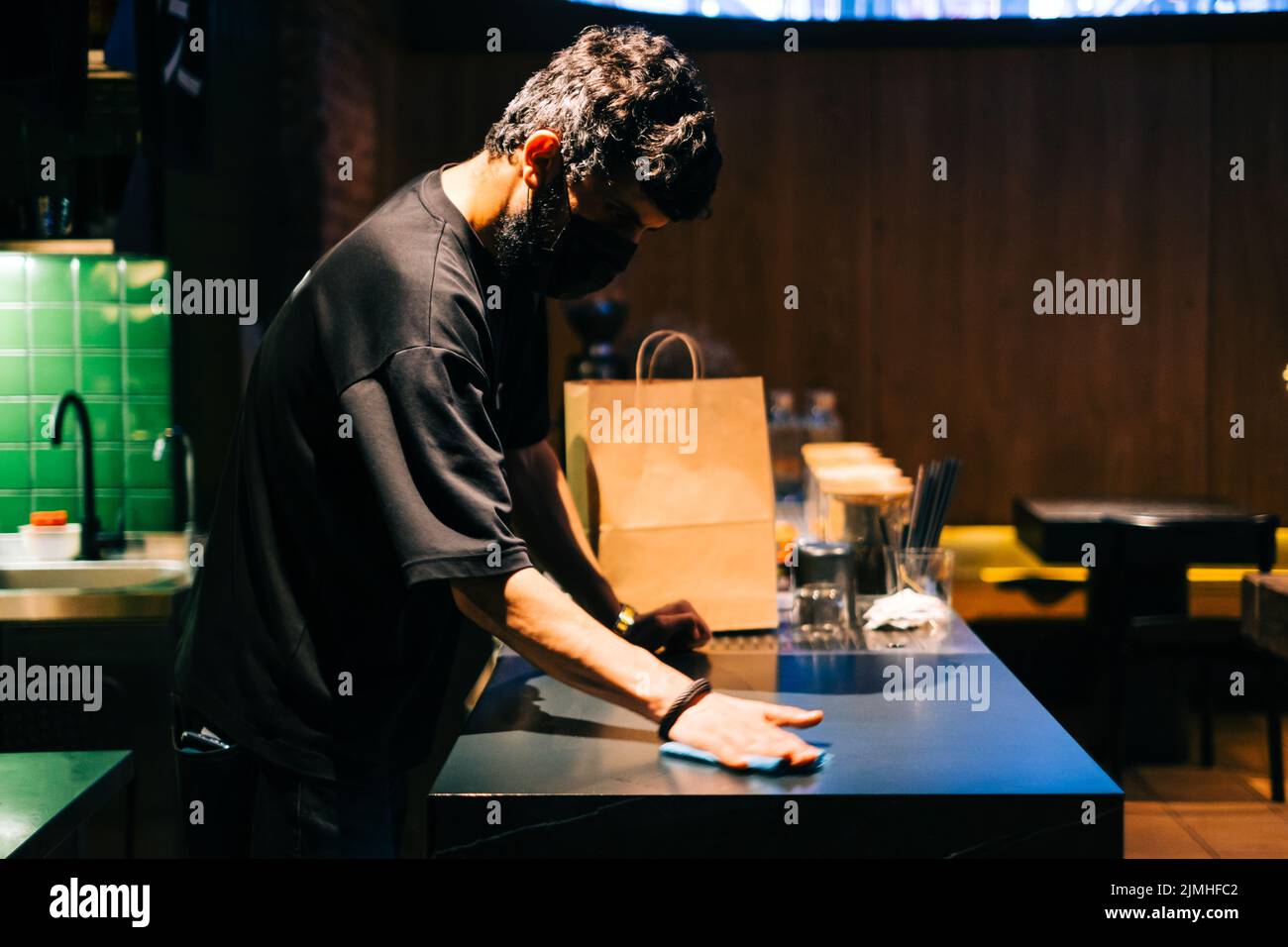 Young caucasian man asian bistro worker cleaning table on the bar ...