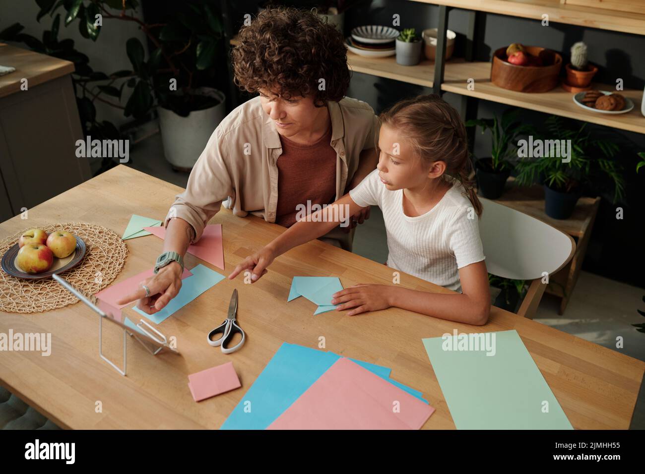 Young woman and her daughter pointing at screen of tablet during online ...