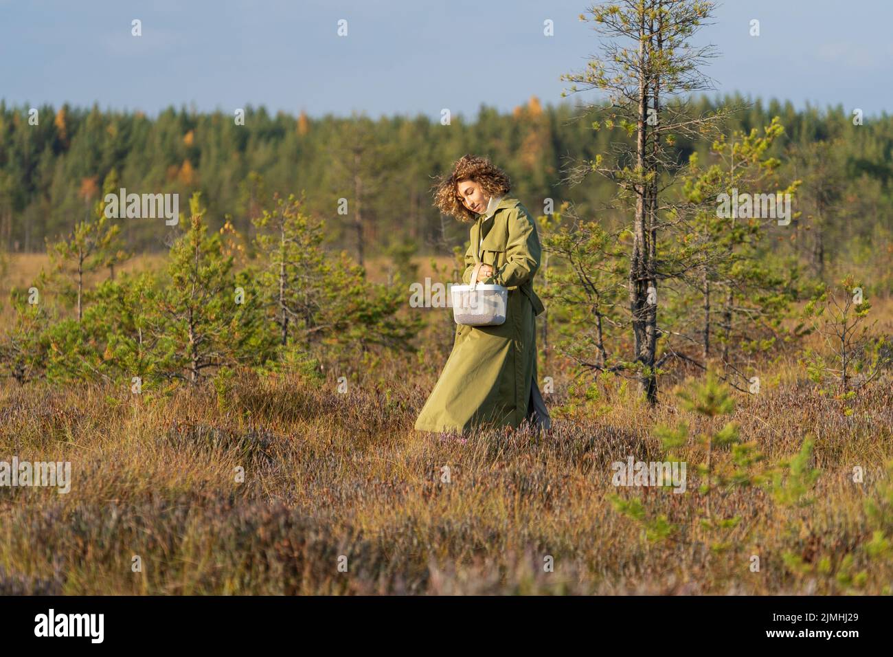 Young woman in trendy trench coat walks across dry swamp searching ...