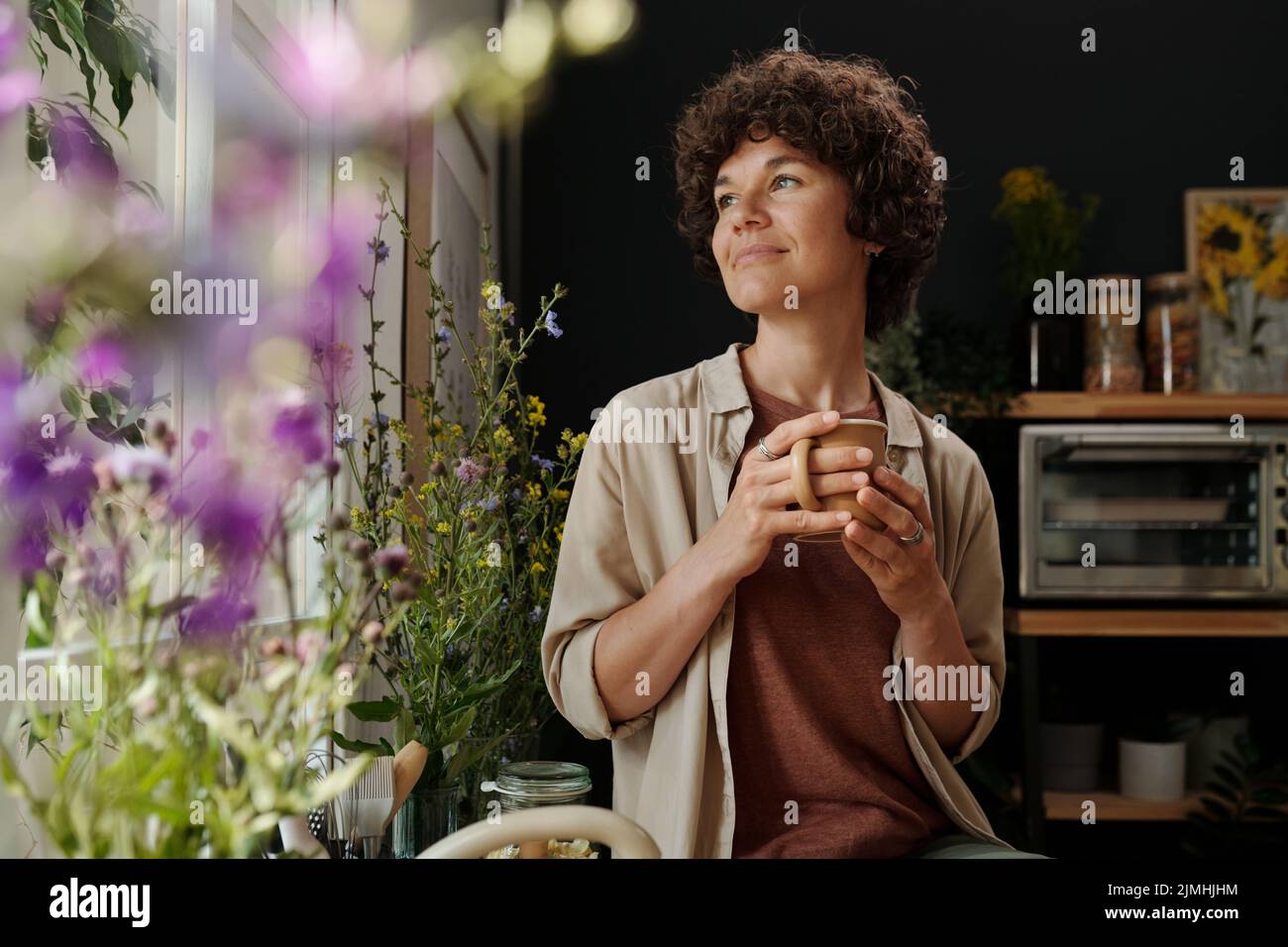 Young contemporary woman in home wear looking through kitchen window ...