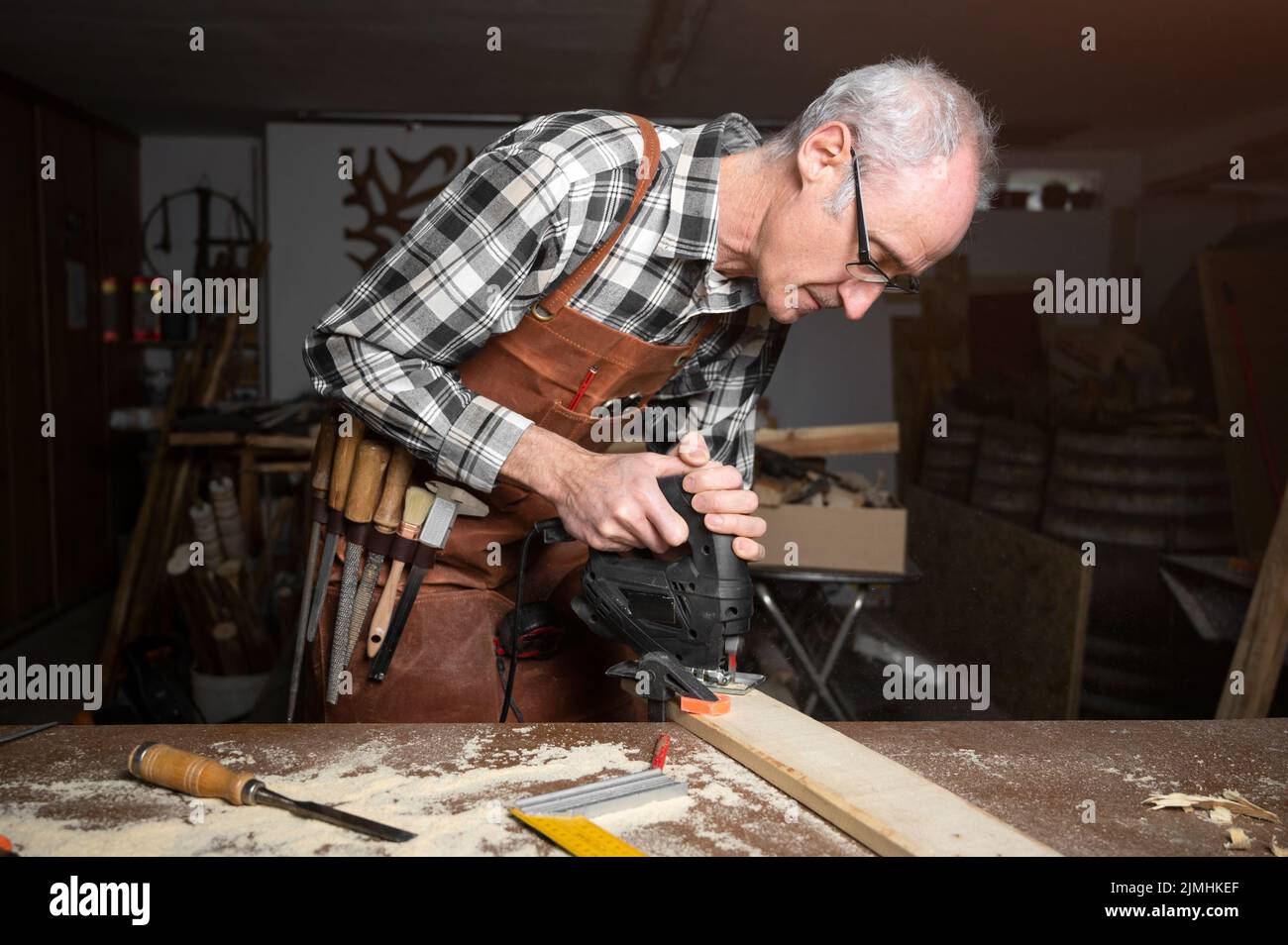 Carpenter is sawing a wood plank with electric jig saw machine in ...