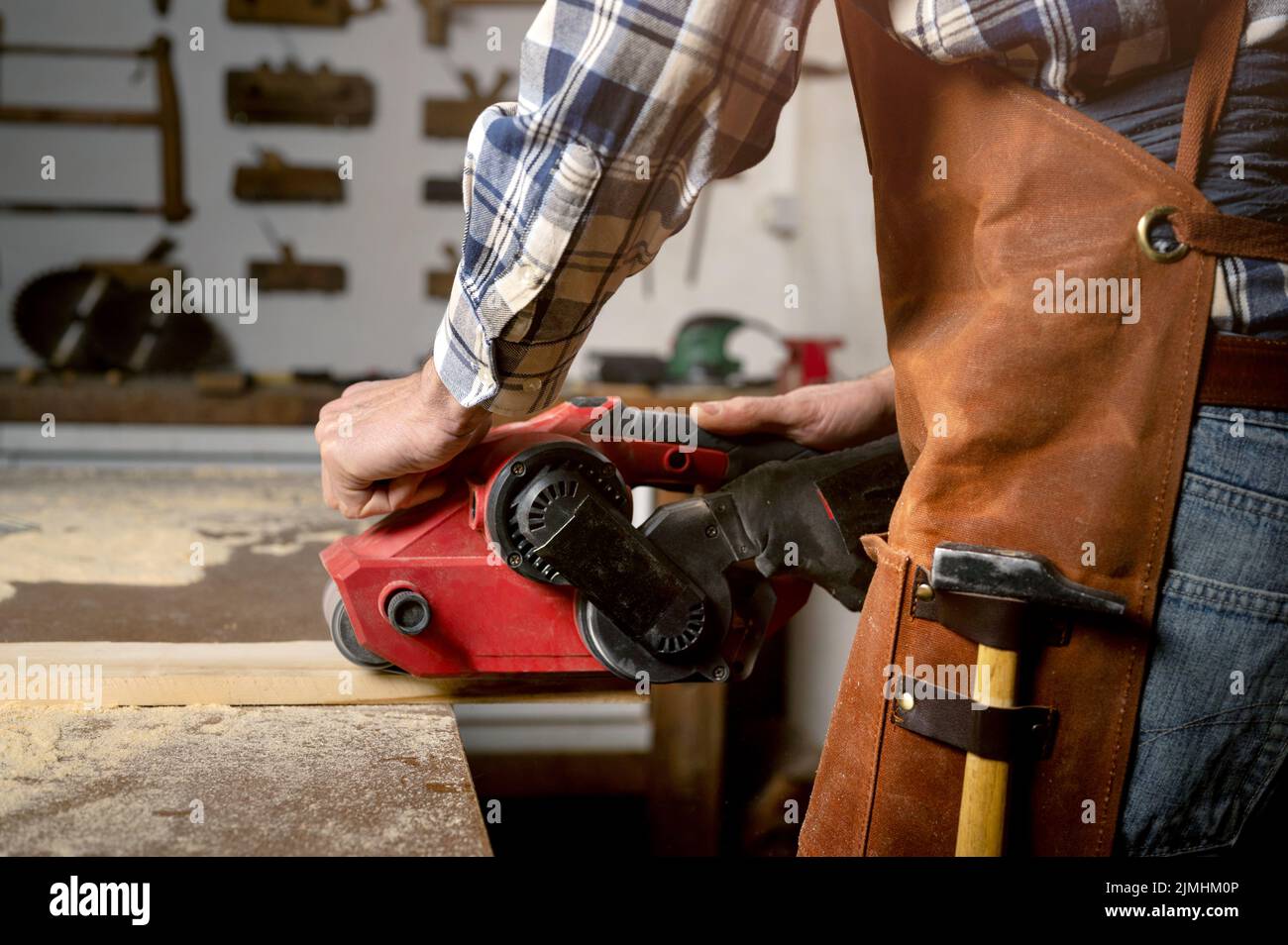 Carpenter sanding wood with belt sander at workshop in wooden board ...