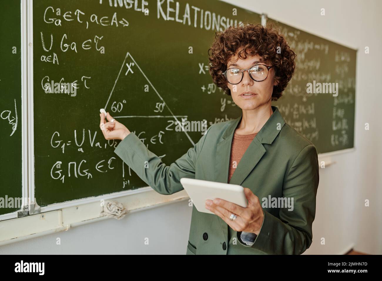 Confident teacher of geometry pointing at triangle on blackboard drawn ...