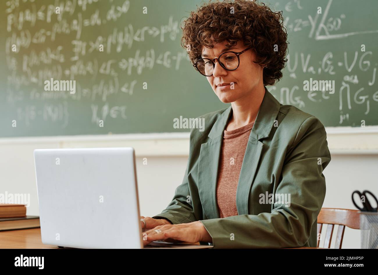 Young confident teacher typing on laptop keypad while sitting by ...