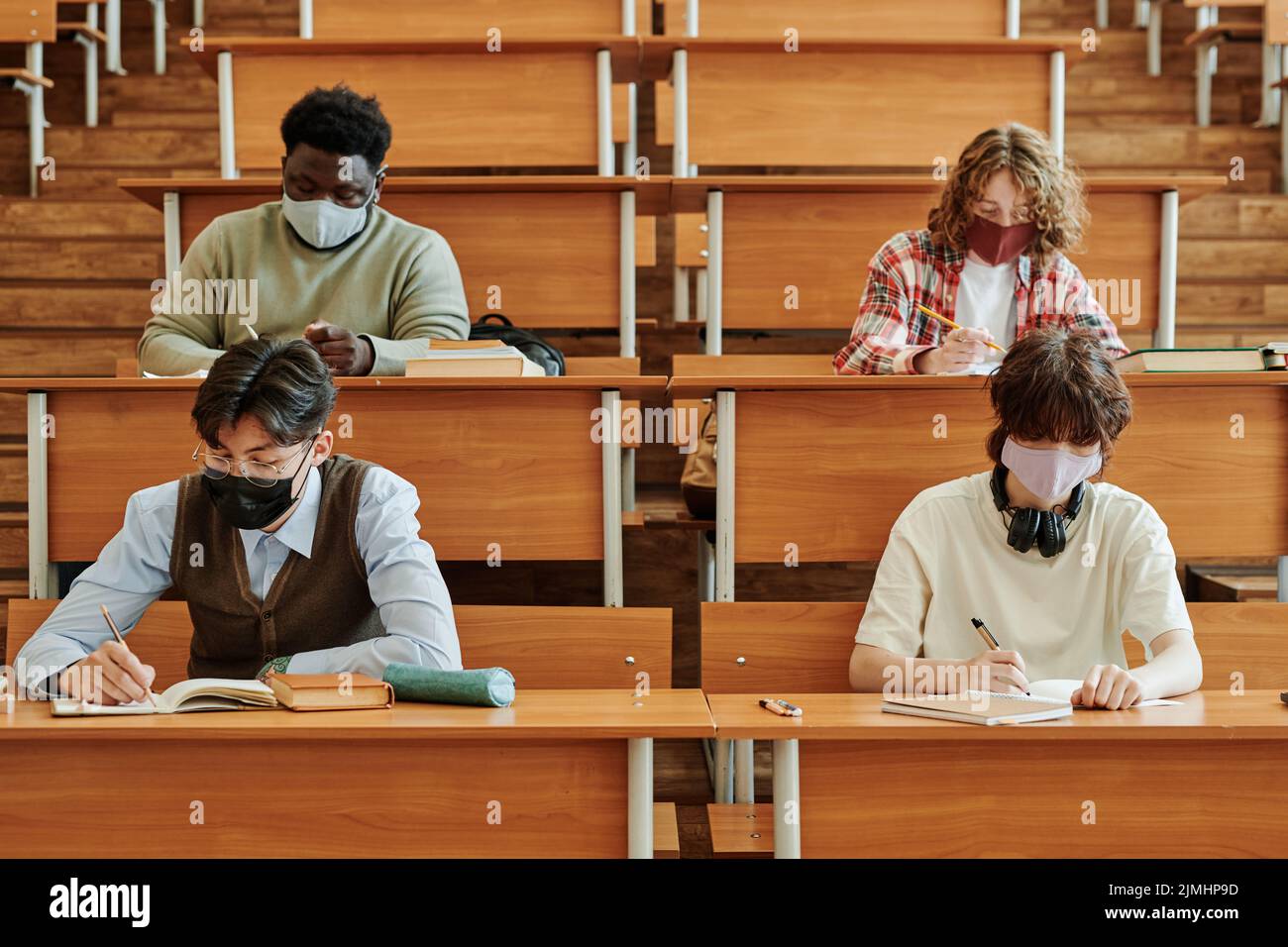 Group of teenage students in protective masks carrying out individual ...