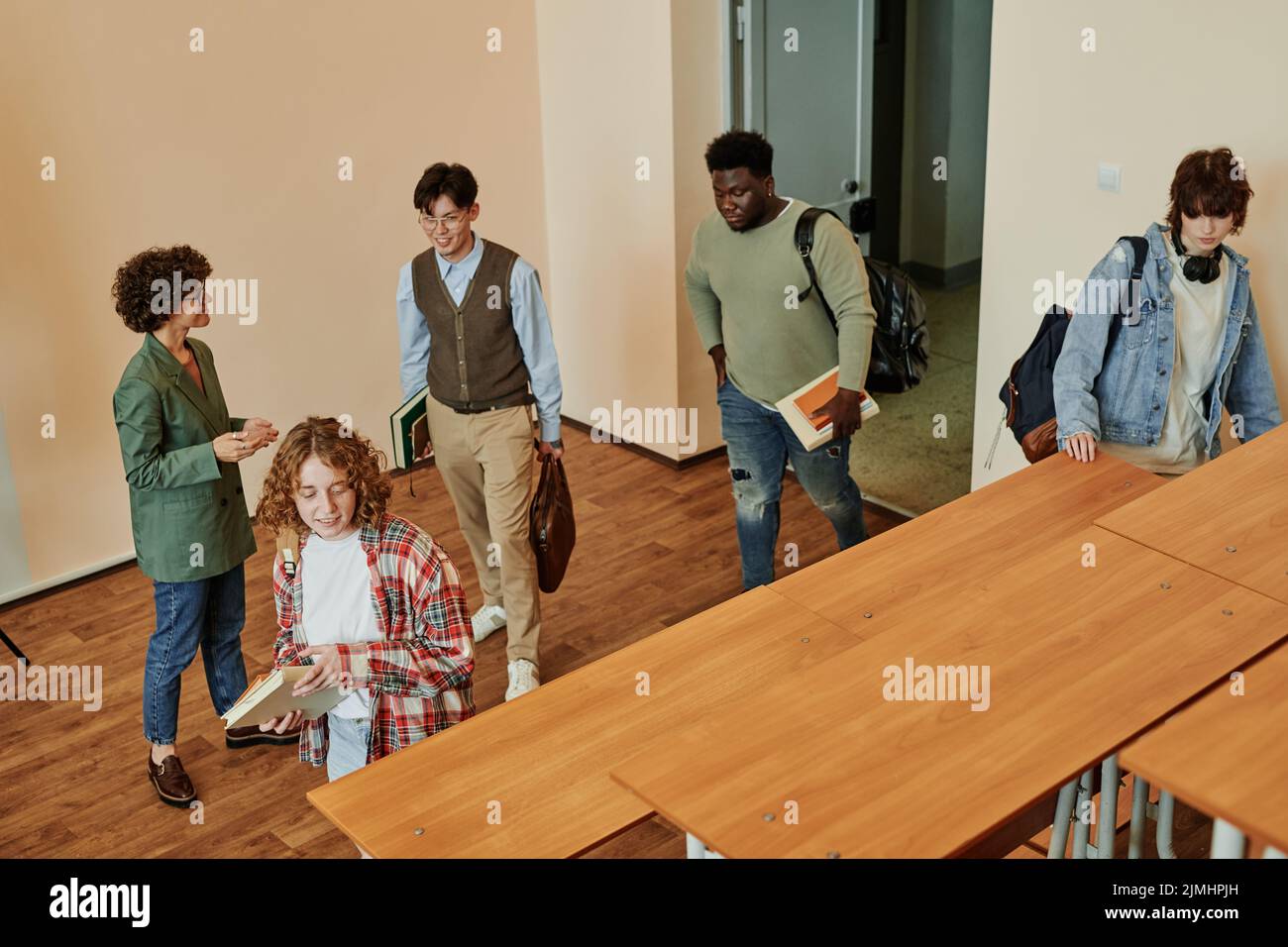 Teacher in smart casualwear standing in front of open door and meeting ...