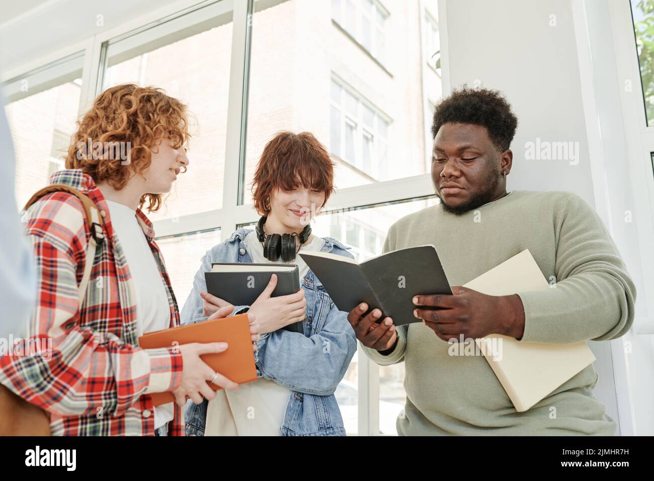 African American guy and two teenage girls looking through lecture ...