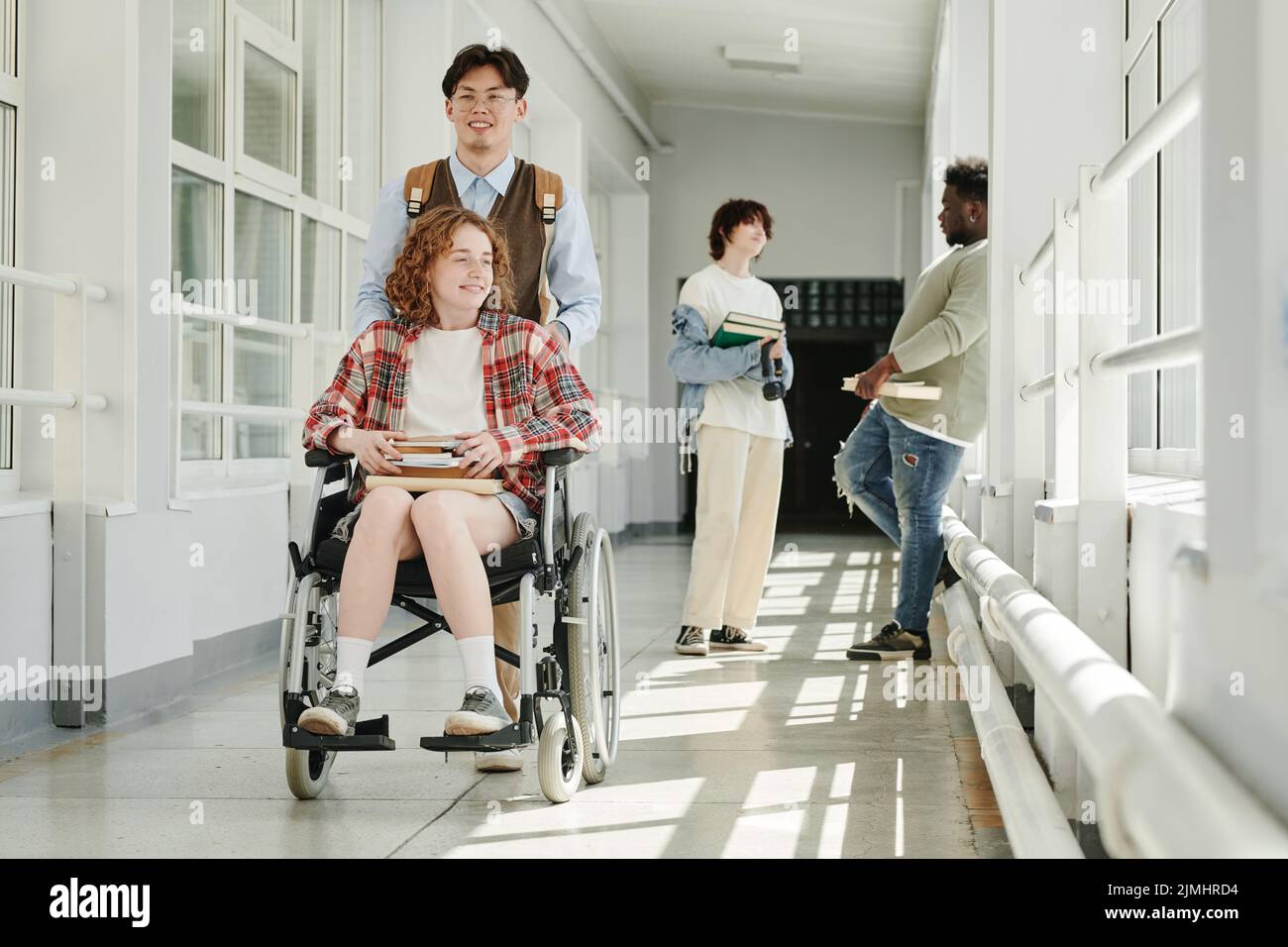 Happy Asian teenager pushing his girlfriend in wheelchair along college ...