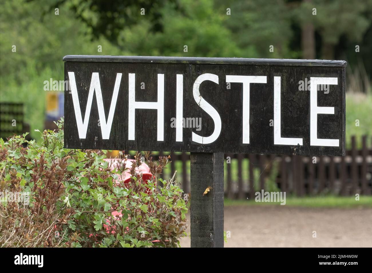 A black railroad whistle sign in Bressingham, UK, against a green leafy ...