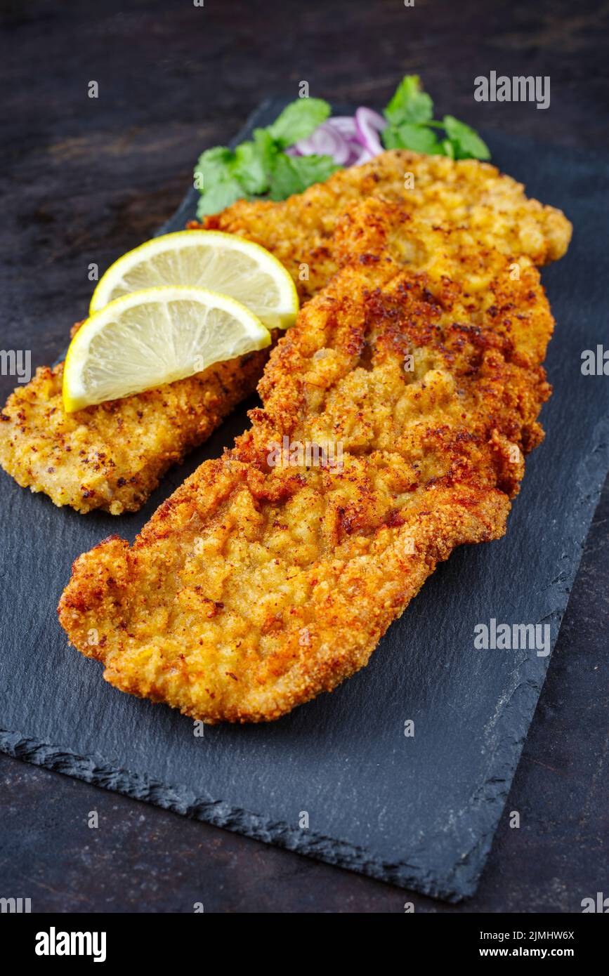 Traditional deep-fried schnitzel with lemon slices and onion rings ...