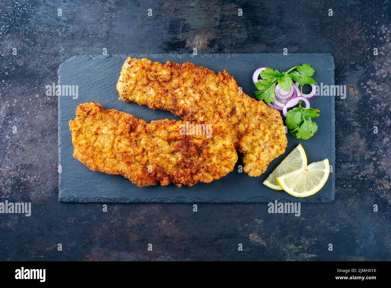 Traditional deep-fried schnitzel with lemon slices and onion rings ...