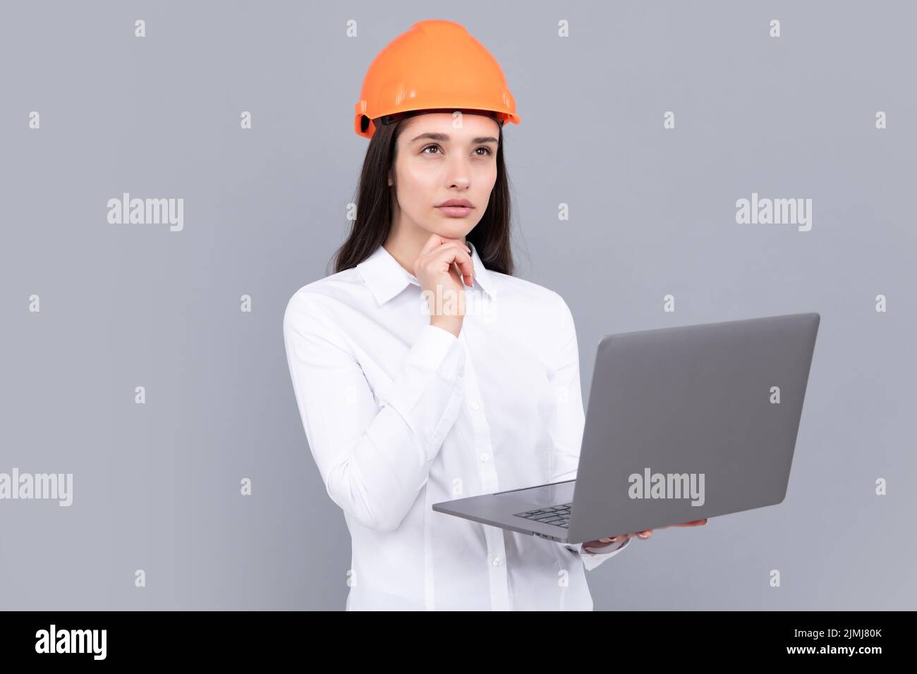 Young woman in hard hat helmet with laptop computer isolated on grey ...