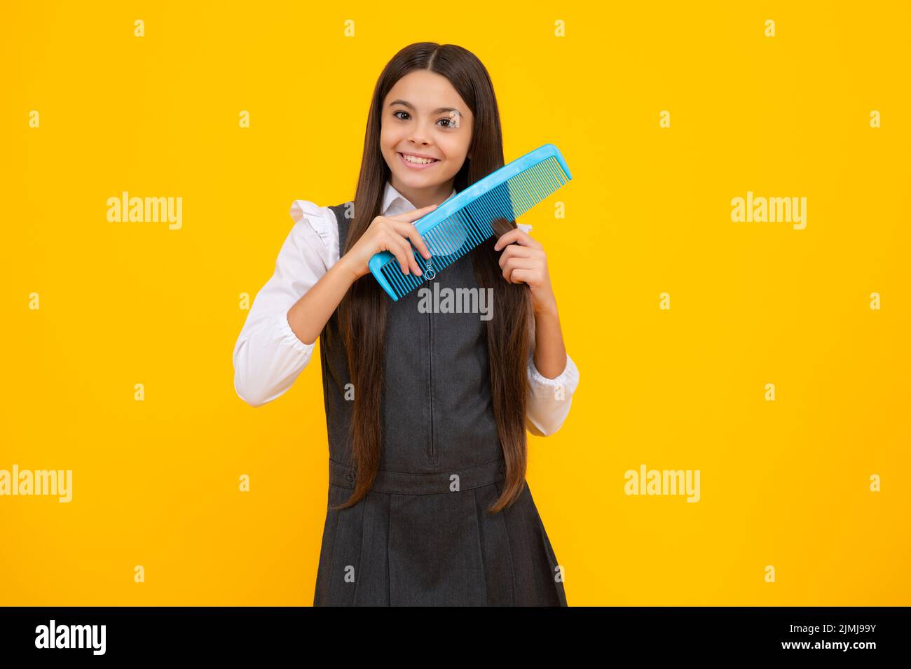 Child brushing combing hair with big comb on yellow isolated studio ...