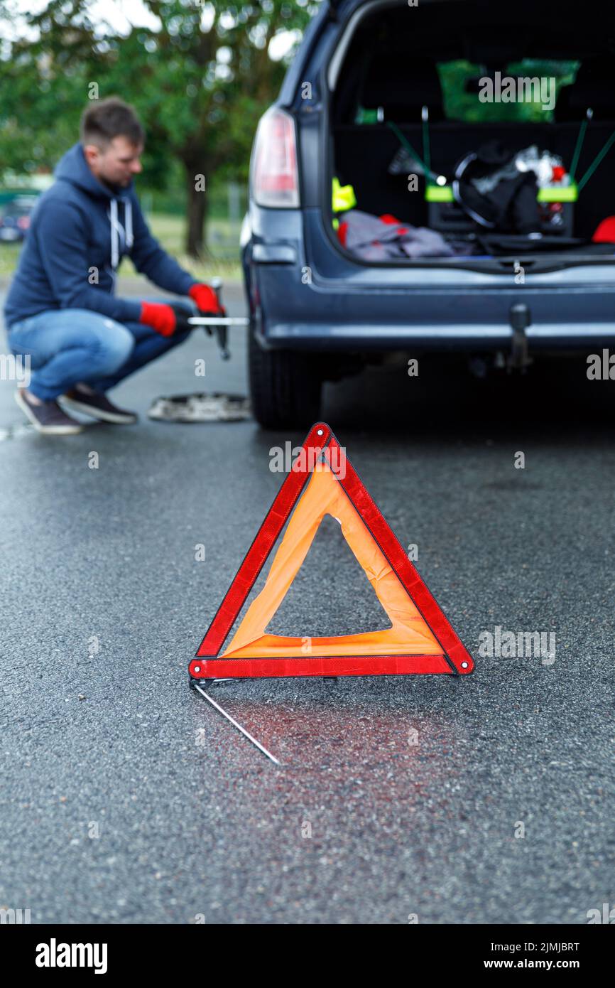 Warning triangle and man changing car wheel Stock Photo - Alamy