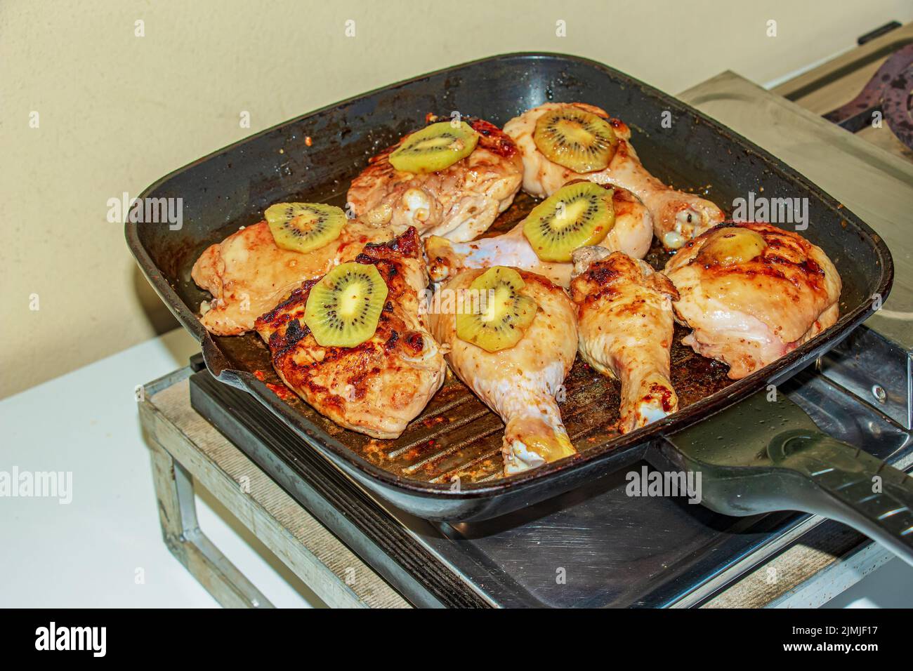Meat with kiwi fruit. Fried chicken pieces with kiwi slices on a grill ...