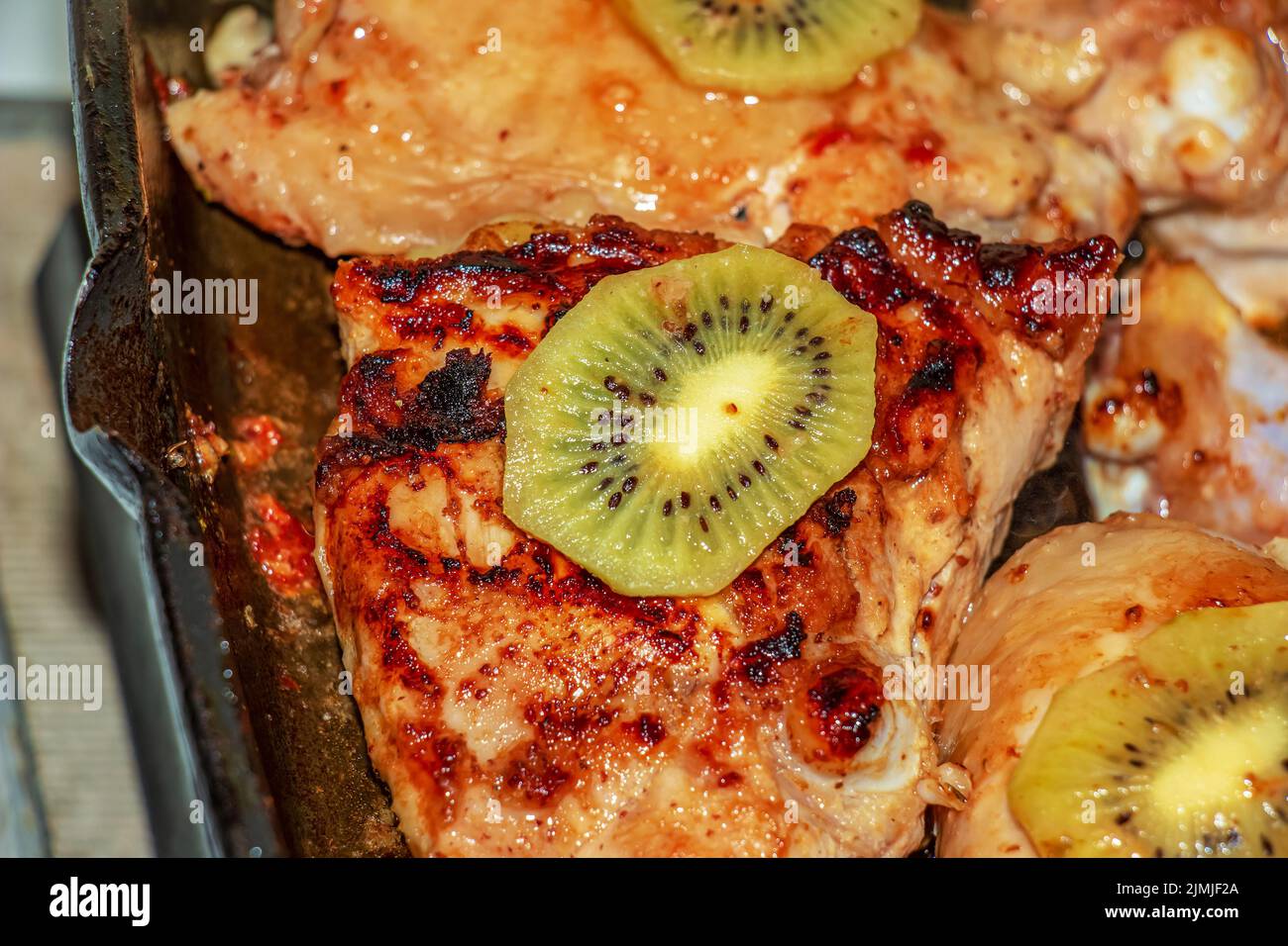 Meat with kiwi fruit. Fried chicken pieces with kiwi slices on a grill ...