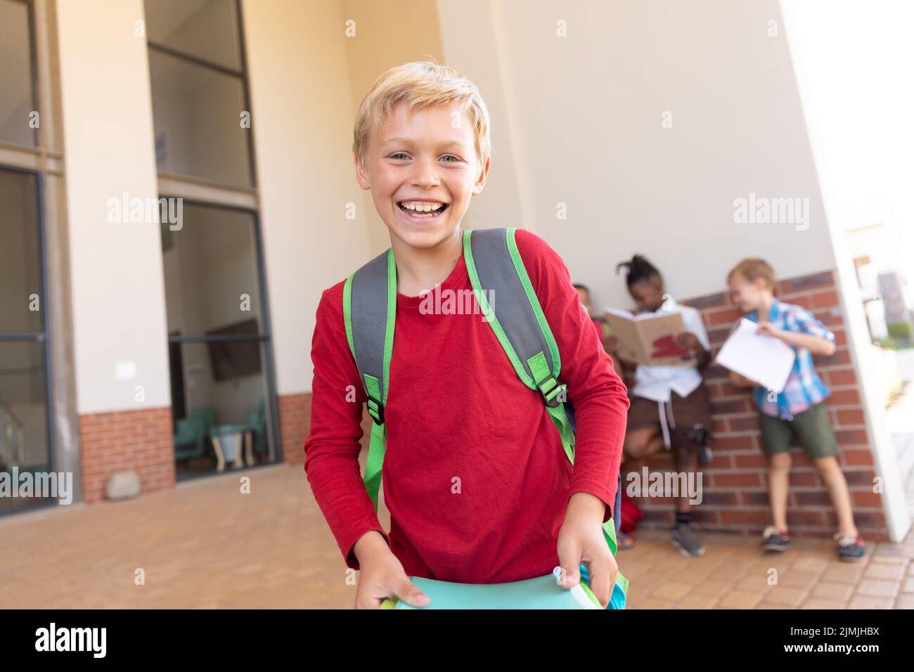 Portrait of cheerful caucasian elementary schoolboy with books standing ...