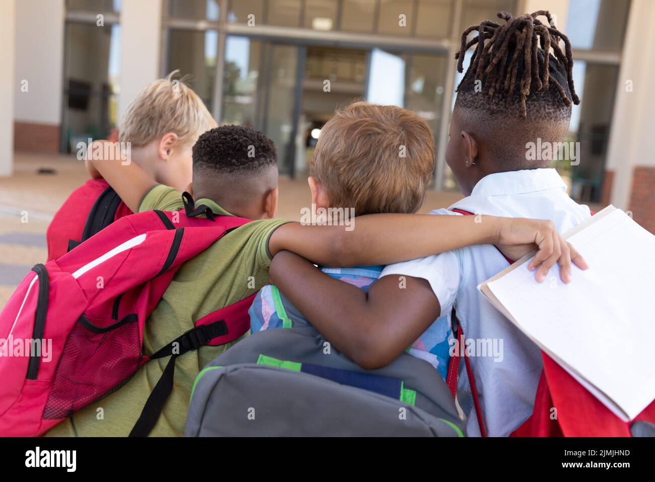 Rear view of multiracial elementary schoolboys with arm around standing ...