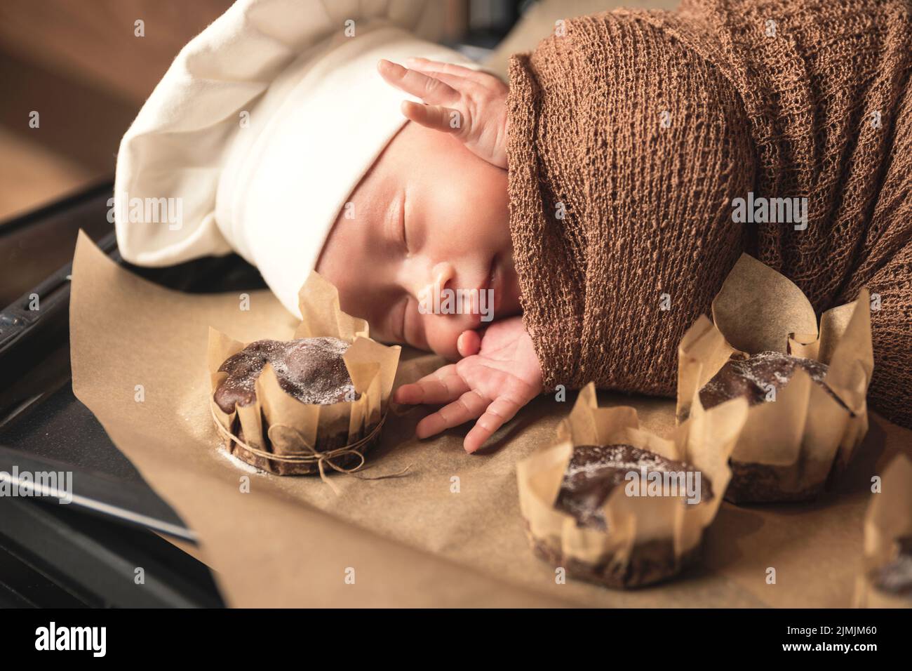 Newborn baby wearing chef's hat is lying on the oven tray with a ...