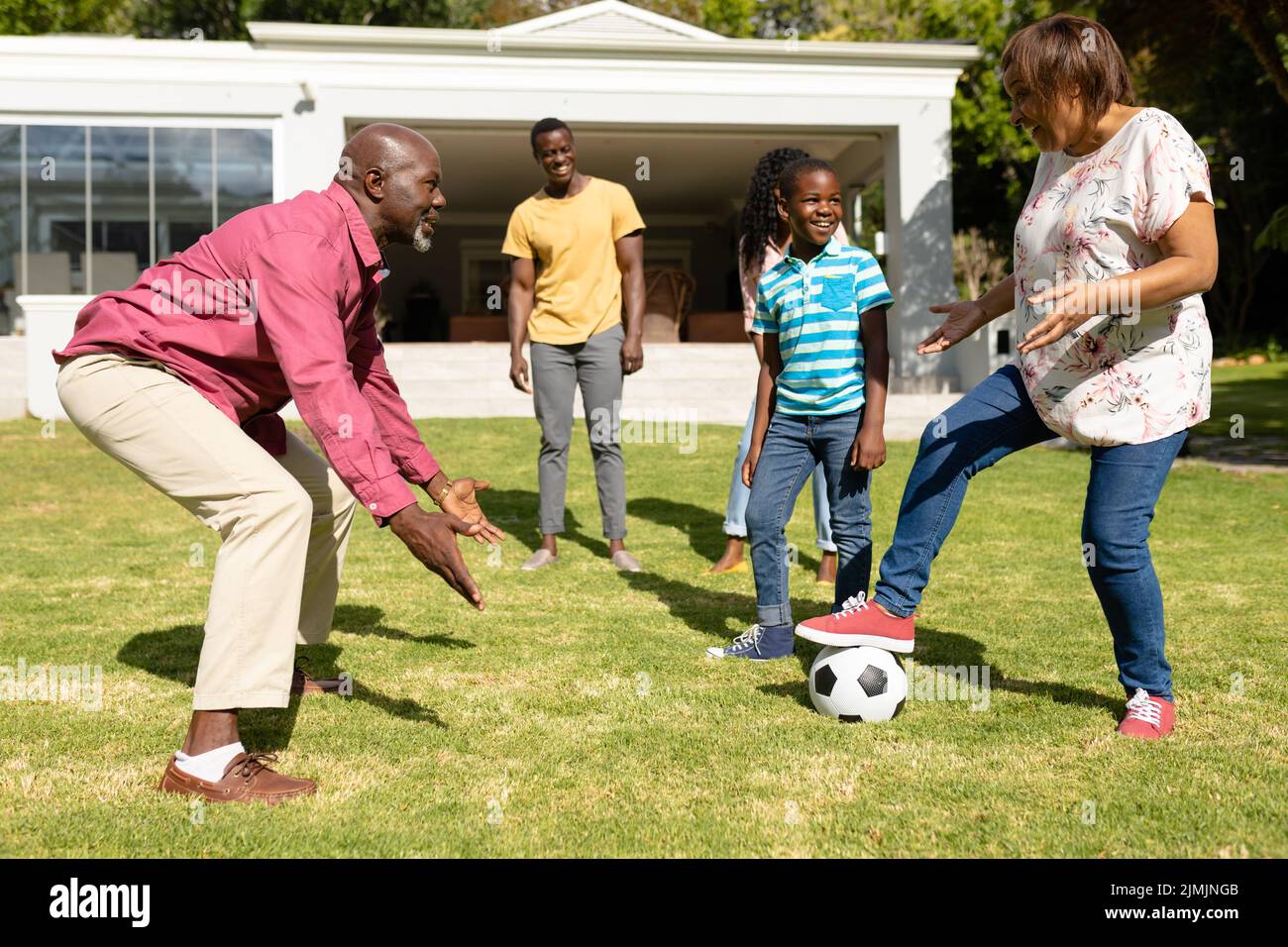 Happy african american multi-generational family playing soccer together in front yard on sunny ...